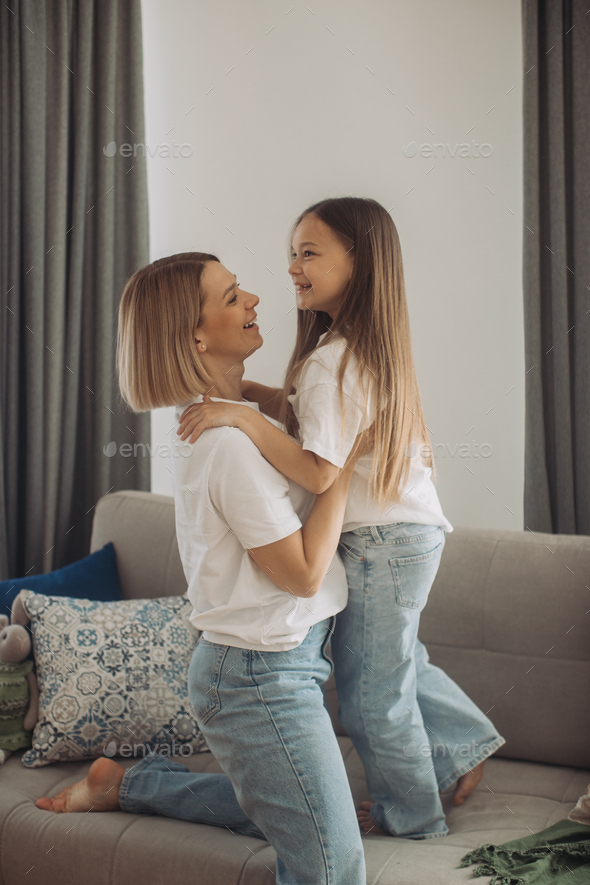 Cheerful mom playing laughing with little daughter on sofa. Stock Photo by dmytros9